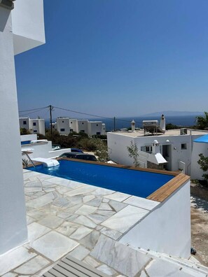 Piscina no terraço com vista clara para o mar e edifícios brancos ao fundo.