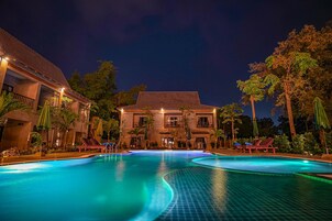 Piscina com espreguiçadeiras e guarda-sóis, cercada por um edifício com telhado telhado e varanda.