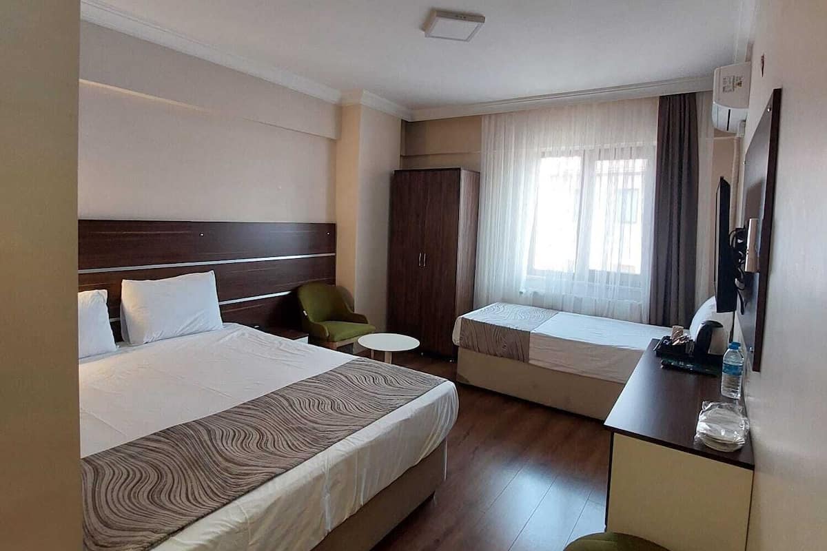 Quarto de hotel com uma cama grande, uma escrivaninha, uma cadeira, um guarda-roupa e uma janela com cortinas.