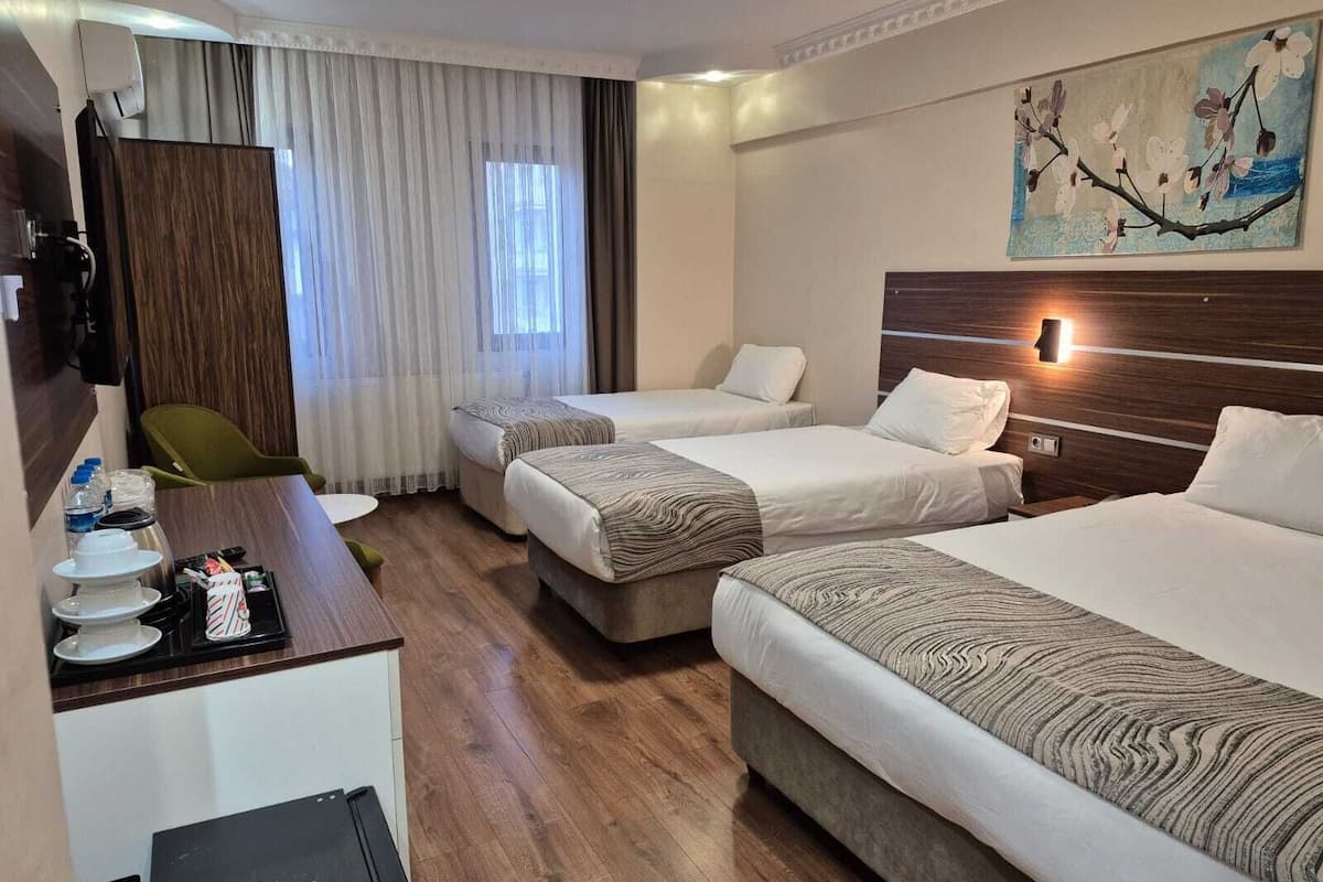 Quarto de hotel com duas camas, uma escrivaninha com cadeira, um quadro na parede e uma janela com cortinas.