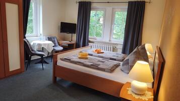 Quarto de hotel com cama, escrivaninha, cadeira, televisão e janela com cortinas.