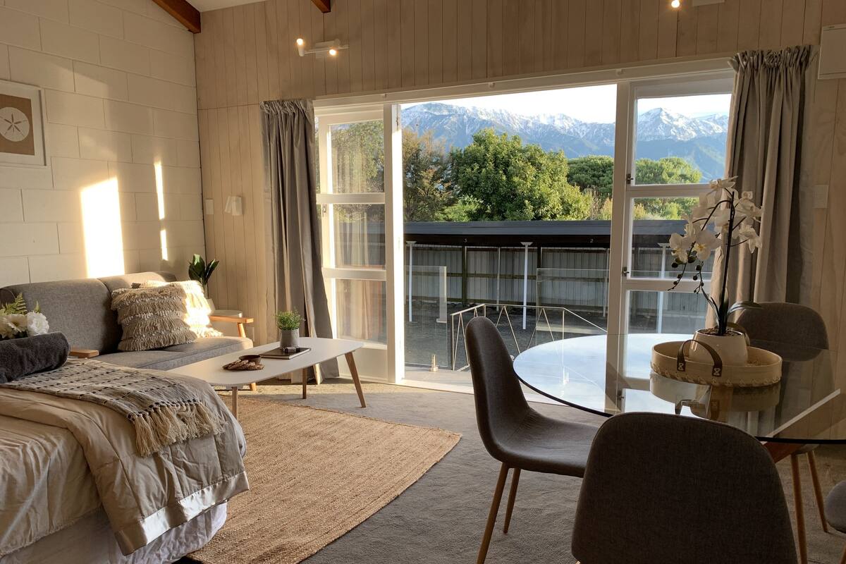 Quarto moderno com uma cama grande, uma mesa de vidro e vista para montanhas pela janela.
