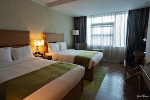 Quarto de hotel com duas camas, uma escrivaninha, uma cadeira e uma janela com cortinas.