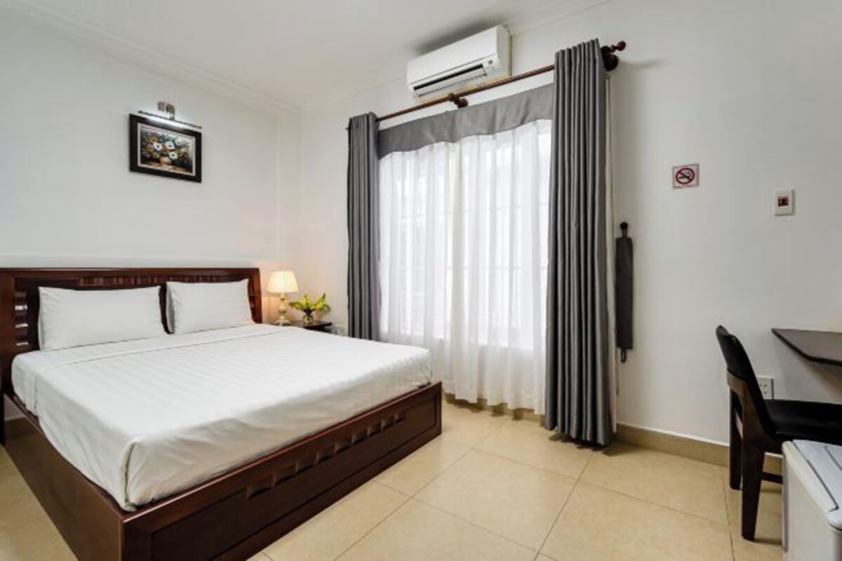 Quarto de hotel com cama, escrivaninha, cadeira, ar condicionado e um quadro na parede.