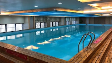 Piscina interior com deck de madeira e guarda-corpos de segurança.
