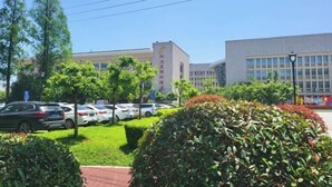 Um estacionamento com vários carros, um edifício com um letreiro e algumas áreas verdes.