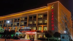 Um hotel com vários andares, iluminado por uma luz quente, e uma placa destacada indicando que é um hotel internacional de cinco estrelas.