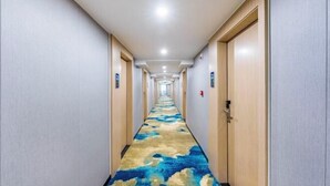 Um corredor de hotel com carpete estampado, portas em ambos os lados e uma longa extensão que leva a um final iluminado.