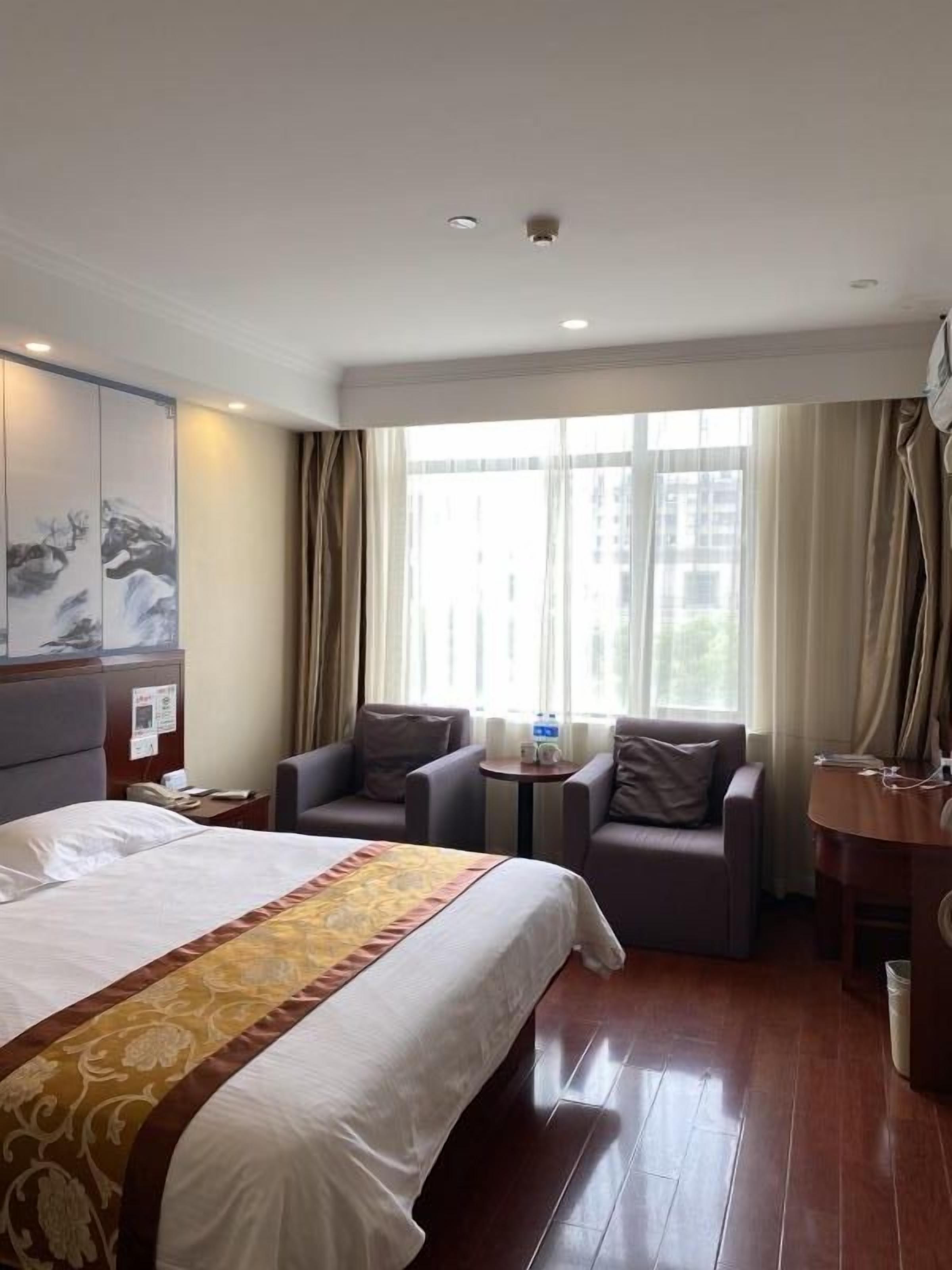 Quarto de hotel com uma cama grande, uma escrivaninha, uma cadeira e janela com cortinas.
