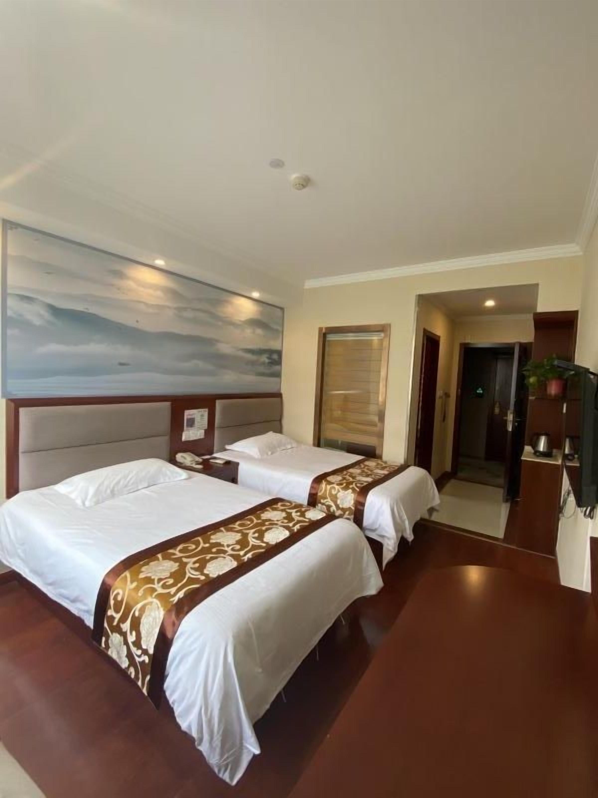 Quarto de hotel com duas camas, um quadro grande na parede e vista para o corredor.