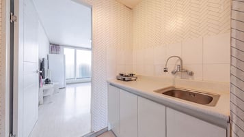 Cozinha moderna com armários brancos, pia de aço inoxidável e backsplash em padrão herringbone.
