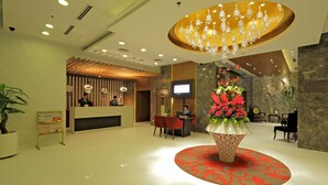 Uma área de recepção de hotel com design moderno, apresentando um balcão de atendimento, área de estar e uma grande peça decorativa.