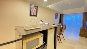 Quarto de hotel compacto com cozinha americana, pia pequena, micro-ondas e área de estar com uma poltrona e um sofá.