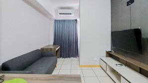 Uma sala de estar com um sofá cinzento, uma mesa de centro de madeira, uma TV de tela plana na parede e um pequeno armário branco.