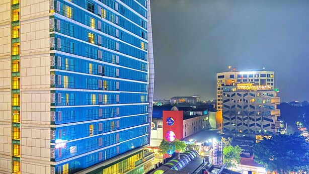 Um hotel moderno com vários andares, grandes janelas e uma placa vermelha bem visível.