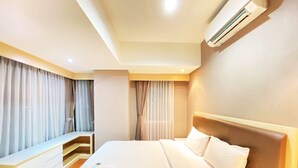 Quarto de hotel com uma cama grande, uma mesinha de cabeceira, um ar condicionado fixado na parede e uma janela com cortinas.
