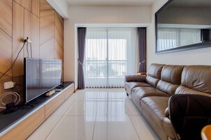 Uma sala de estar moderna com televisão de tela plana, painéis de madeira, sofá de couro e uma janela grande com cortinas translúcidas.