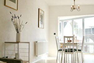 Um quarto iluminado com uma mesa de jantar e cadeiras, um radiador e um vaso com plantas.