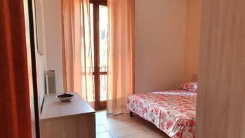 Um quarto com cama, escrivaninha e janela com cortinas.