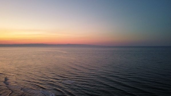 Mar calmo ao pôr do sol, com a linha costeira distante.