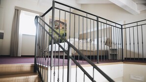 Uma escadaria com corrimão preto leva a um quarto com cama e vista para a paisagem pela janela.