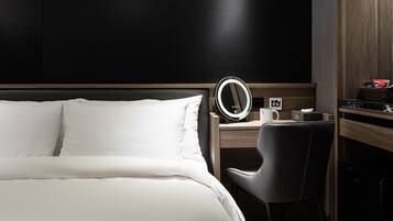 Quarto de hotel com uma cama, uma escrivaninha com um computador, uma cadeira e um espelho redondo.