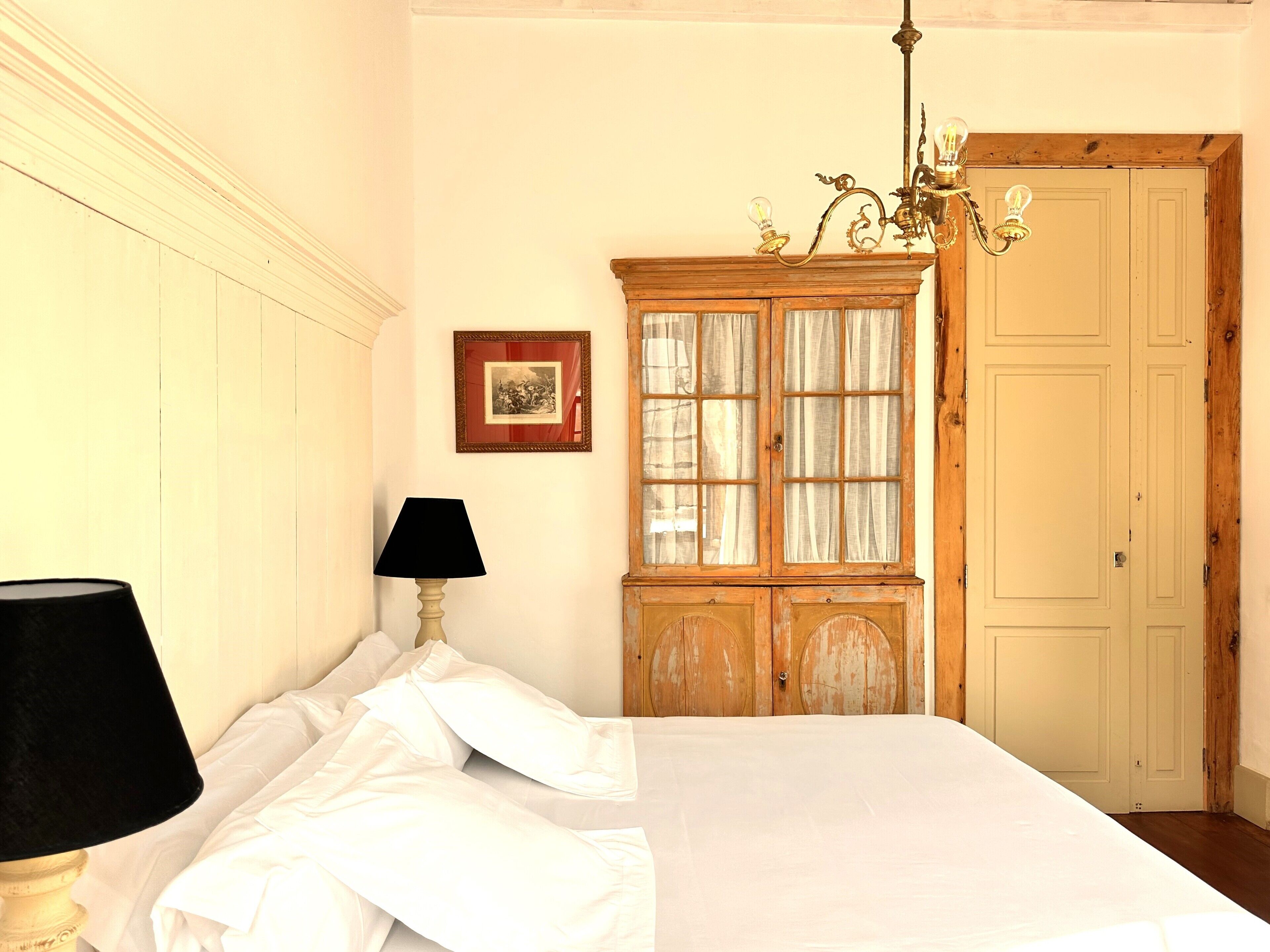Um quarto com uma cama, um armário de madeira, um quadro emoldurado e um candelabro.