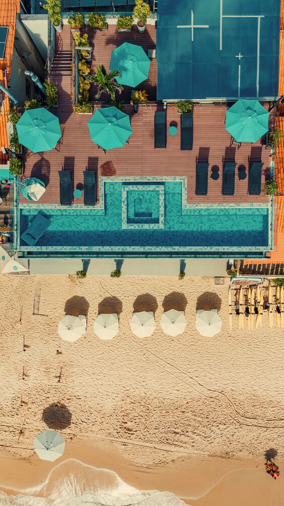 Uma área de piscina no terraço com espreguiçadeiras e guarda-sóis, uma piscina e uma praia com espreguiçadeiras e guarda-sóis.