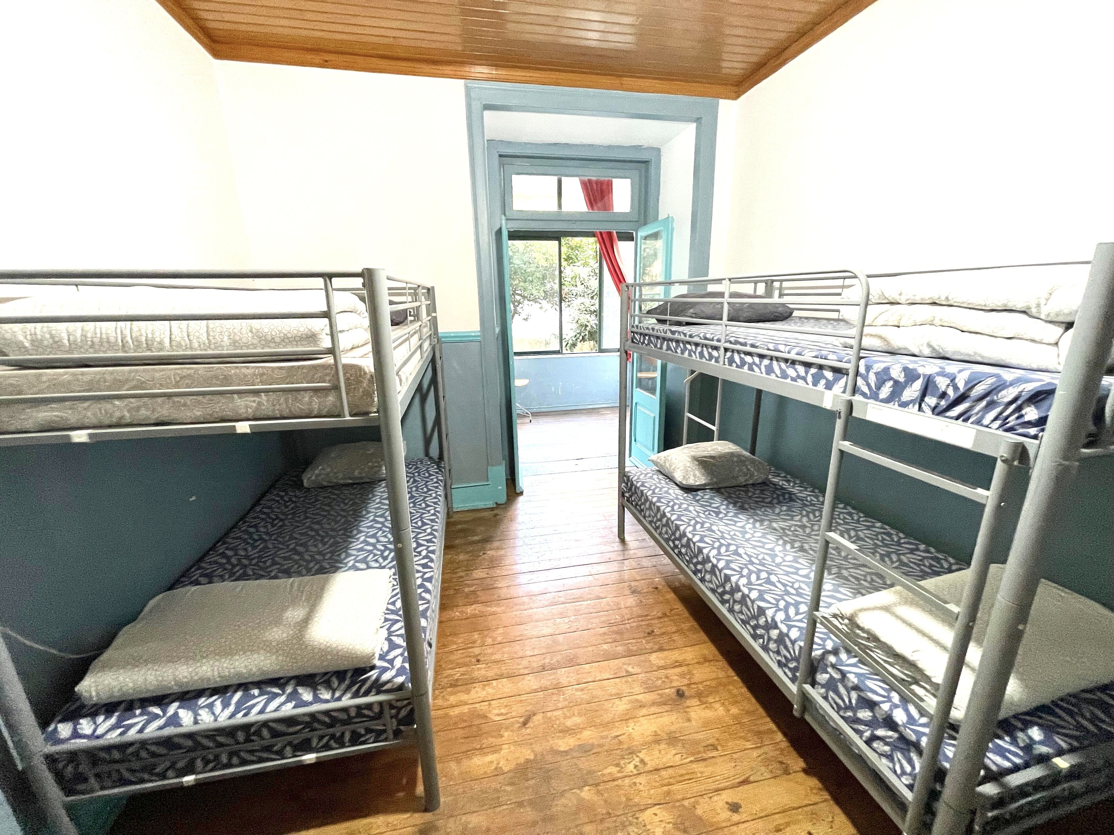 Quarto com beliches, piso de madeira e porta que dá para o exterior.