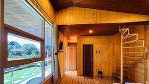 Interior de madeira com escada, uma janela grande e vista para um jardim.