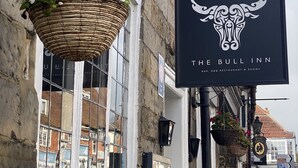 Um edifício com uma placa indicando 'The Bull Inn', exibindo o logotipo de uma cabeça de touro.