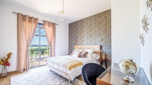 Quarto com cama, escrivaninha com globo, cadeira, janela com cortinas e parede estampada.