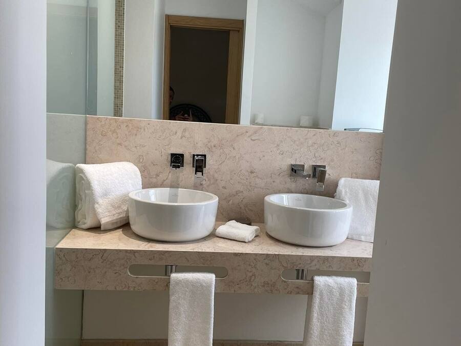 Um banheiro moderno com duas pias grandes brancas, um espelho e um porta-toalhas.