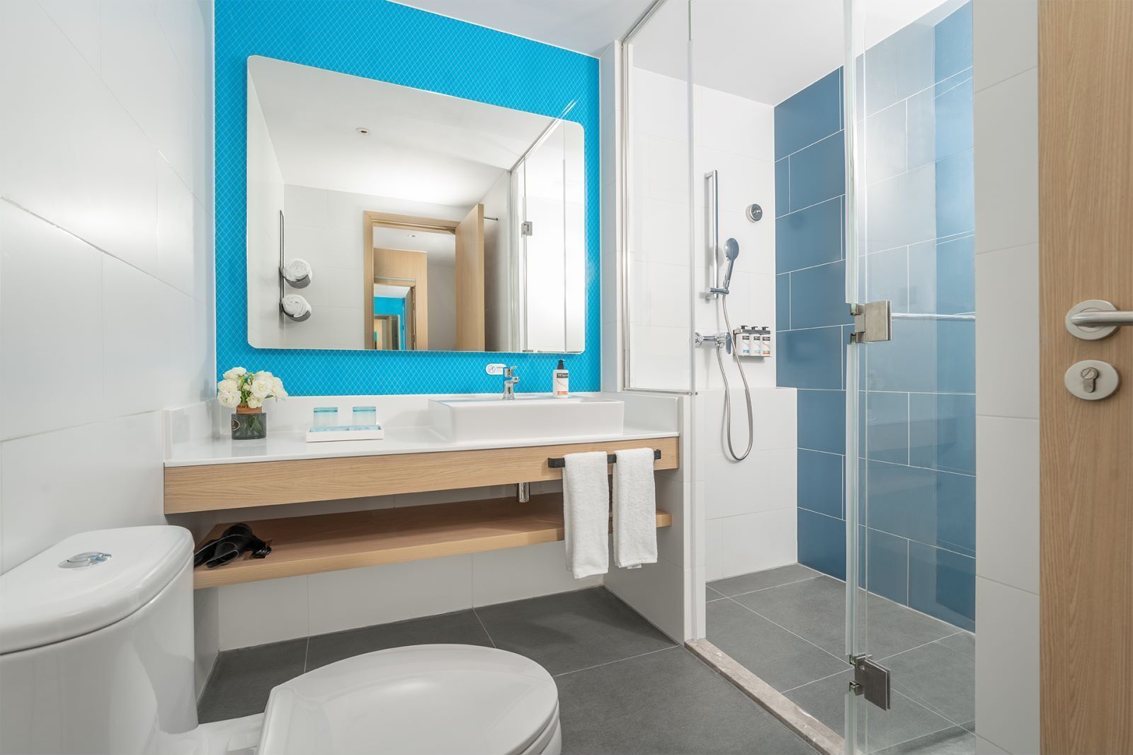 Um banheiro moderno com vaso sanitário branco, pia com painel de azulejos azuis, espelho e chuveiro com box de vidro.