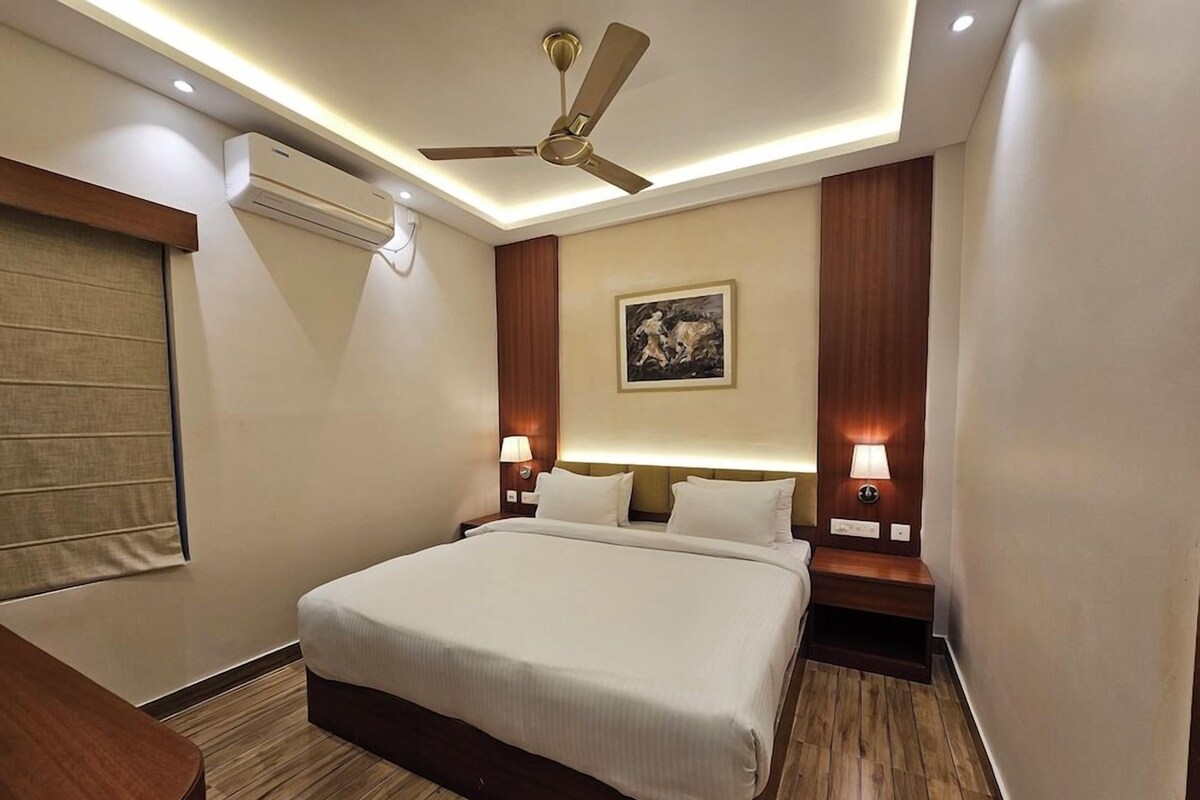 Quarto de hotel com uma cama grande, luminárias de cabeceira, ar condicionado, ventoinha de teto e um quadro na parede.