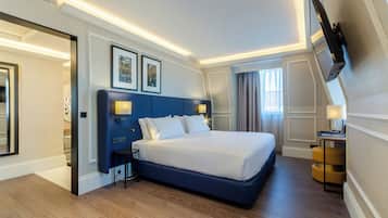 Quarto de hotel com uma cama grande, televisão na parede e uma pequena mesa com abajur.