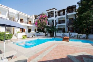 Uma área de piscina com piscina azul translúcida, espreguiçadeiras e um espaço de estar coberto.