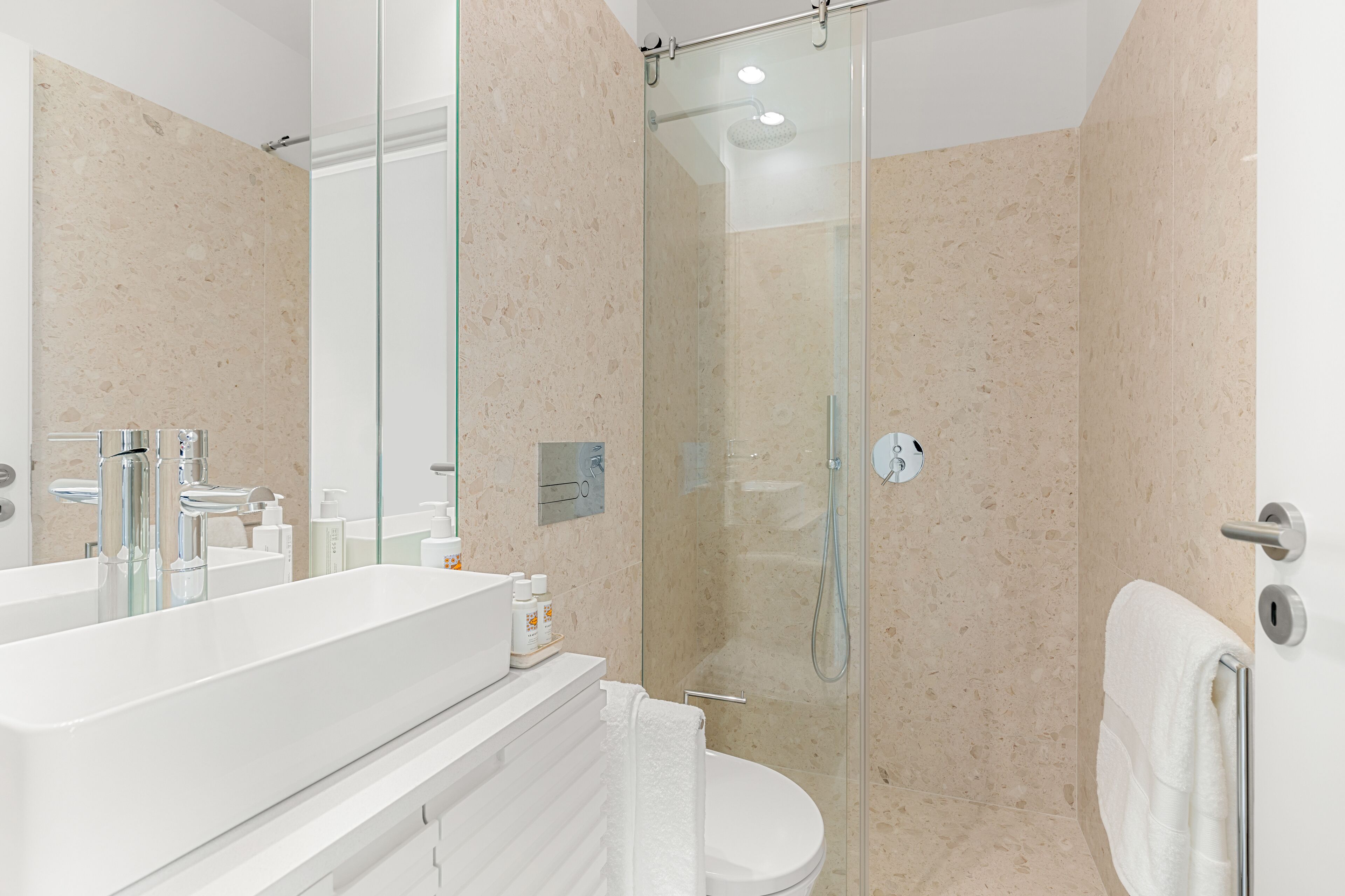 Uma casa de banho moderna com chuveiro envidraçado, lavatório branco e espelho grande.