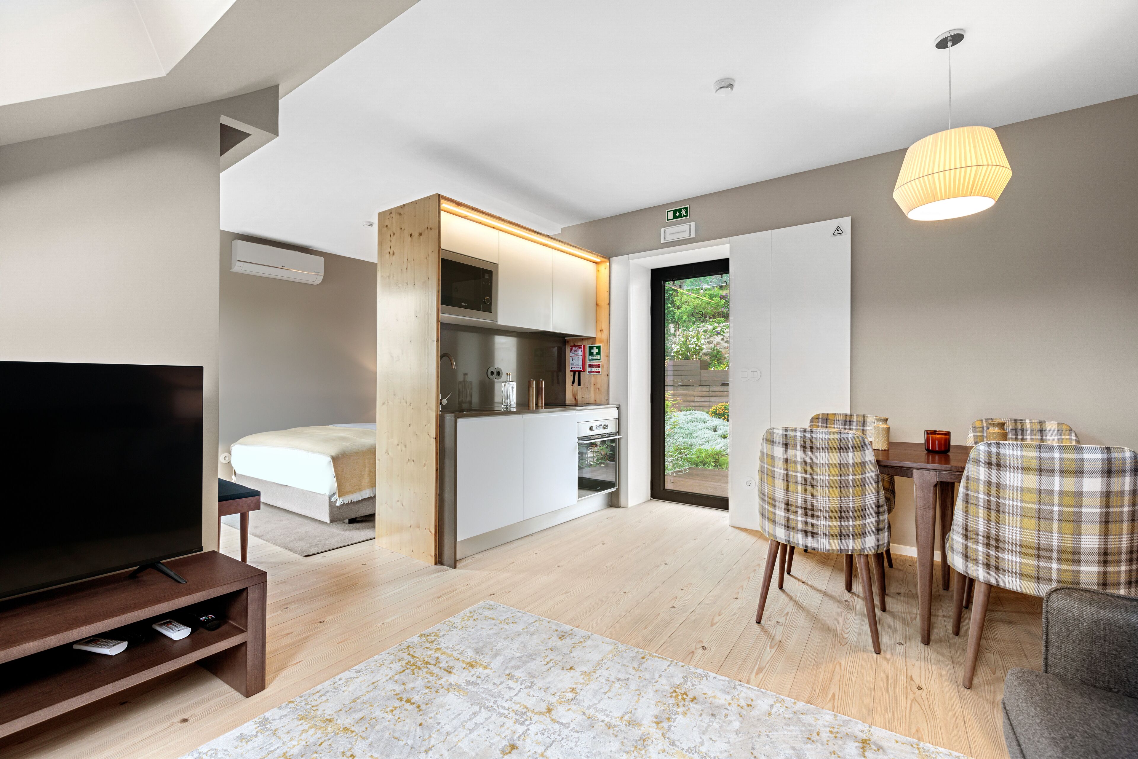 Uma sala de estar moderna com televisão de tela plana, um sofá, uma área de jantar com cadeiras xadrez e uma cozinha com armário de madeira.