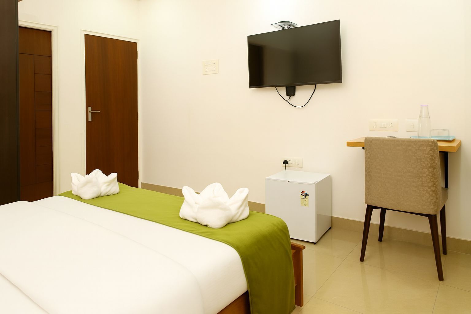 Quarto de hotel com uma cama, escrivaninha, televisão e mini-geladeira.