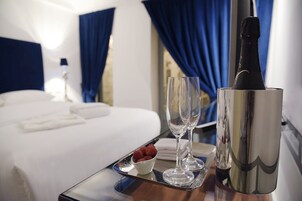 Quarto de hotel com uma cama bem arrumada, uma bandeja com champanhe, duas taças de vinho e uma tigela de framboesas.