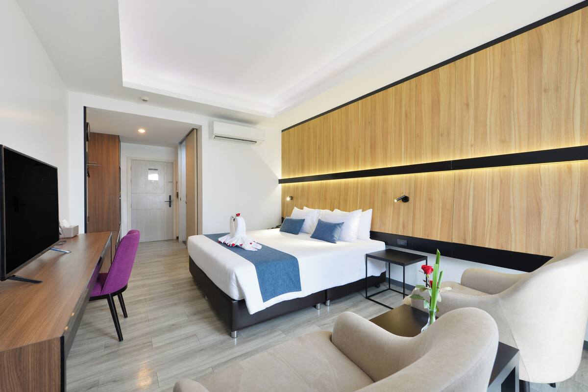 Quarto de hotel moderno com uma cama grande, uma mesa, uma cadeira e um sofá.