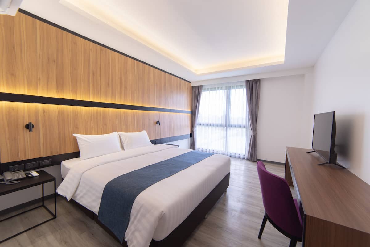 Quarto de hotel moderno com uma cama grande, uma escrivaninha, televisão de tela plana e uma parede de destaque em madeira.
