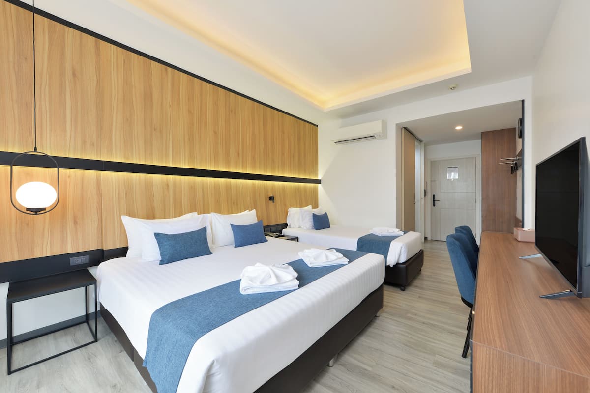 Quarto de hotel com duas camas, uma escrivaninha, uma TV e um painel de parede em madeira.