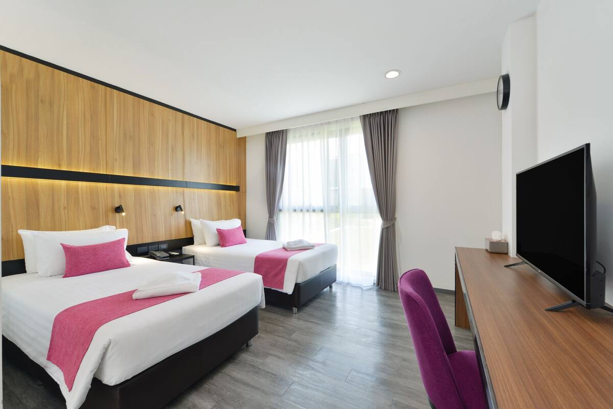 Quarto de hotel com duas camas, televisão, escrivaninha e cadeira.