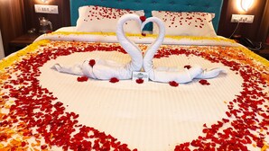 Quarto de hotel com cama decorada com pétalas de rosa e arranjo de toalha em formato de cisne.