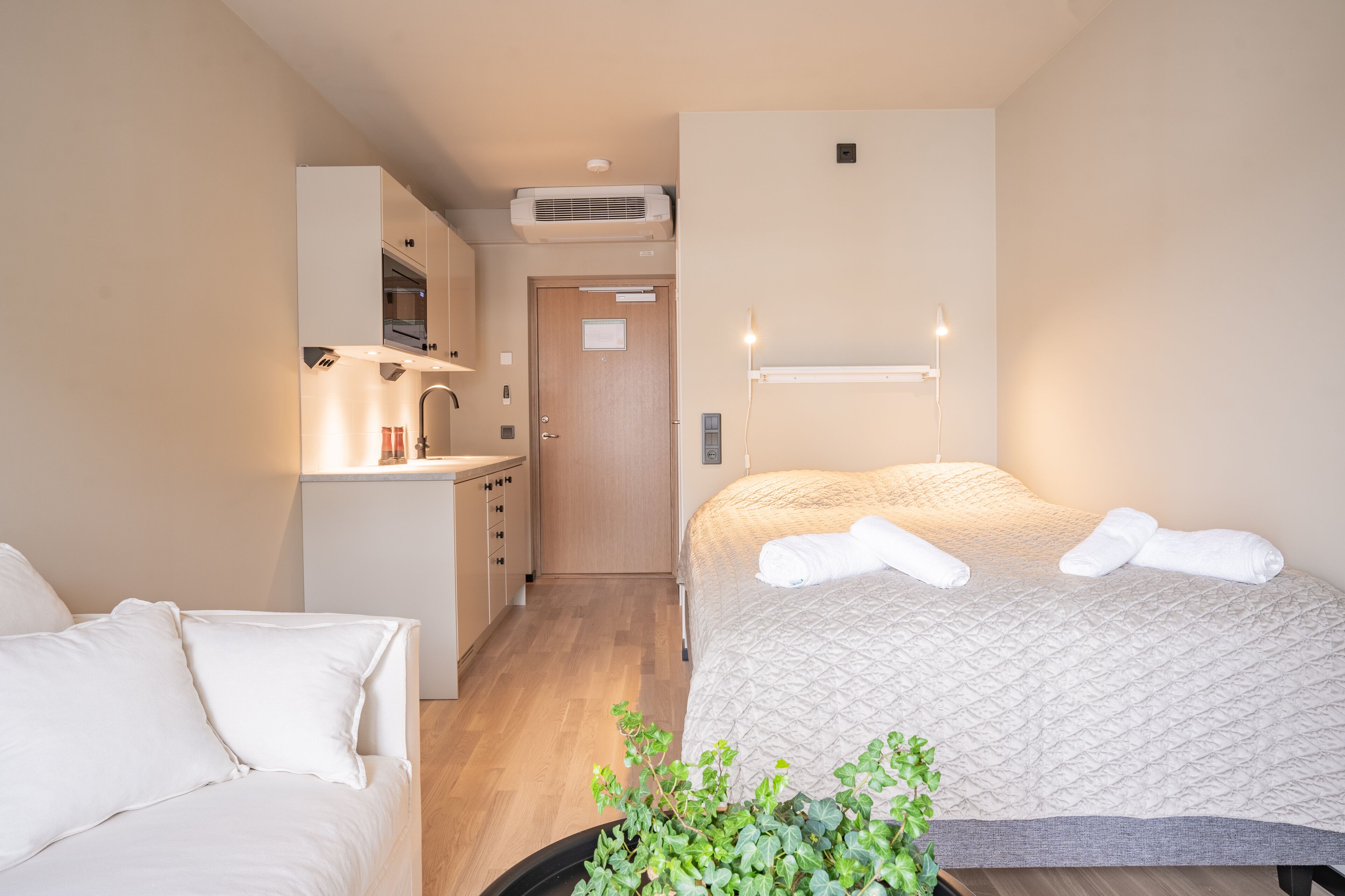 Quarto de hotel com cama, uma kitchenette compacta, banheiro e planta em vaso.