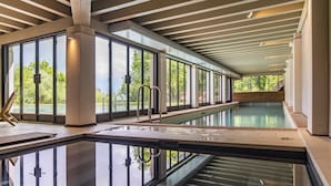 Piscina com paredes de vidro transparente, chão ladrilhado e teto com vigas aparentes.