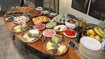 Uma mesa de buffet com diversos queijos, carnes, frutas e doces.