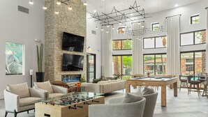Uma sala de estar ampla com mesa de futebol, assentos confortáveis, lareira e grandes janelas com vista para o exterior.